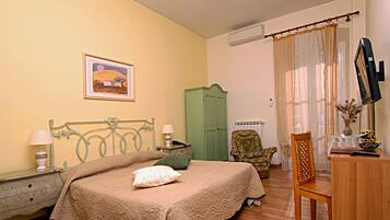 Um quarto com uma cama, um guarda-roupa verde, uma cadeira de madeira, uma escrivaninha com um vaso e uma televisão.