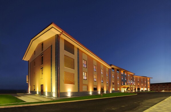 Um hotel grande e de vários andares, com design moderno, destacando uma entrada imponente e fachada bem iluminada.