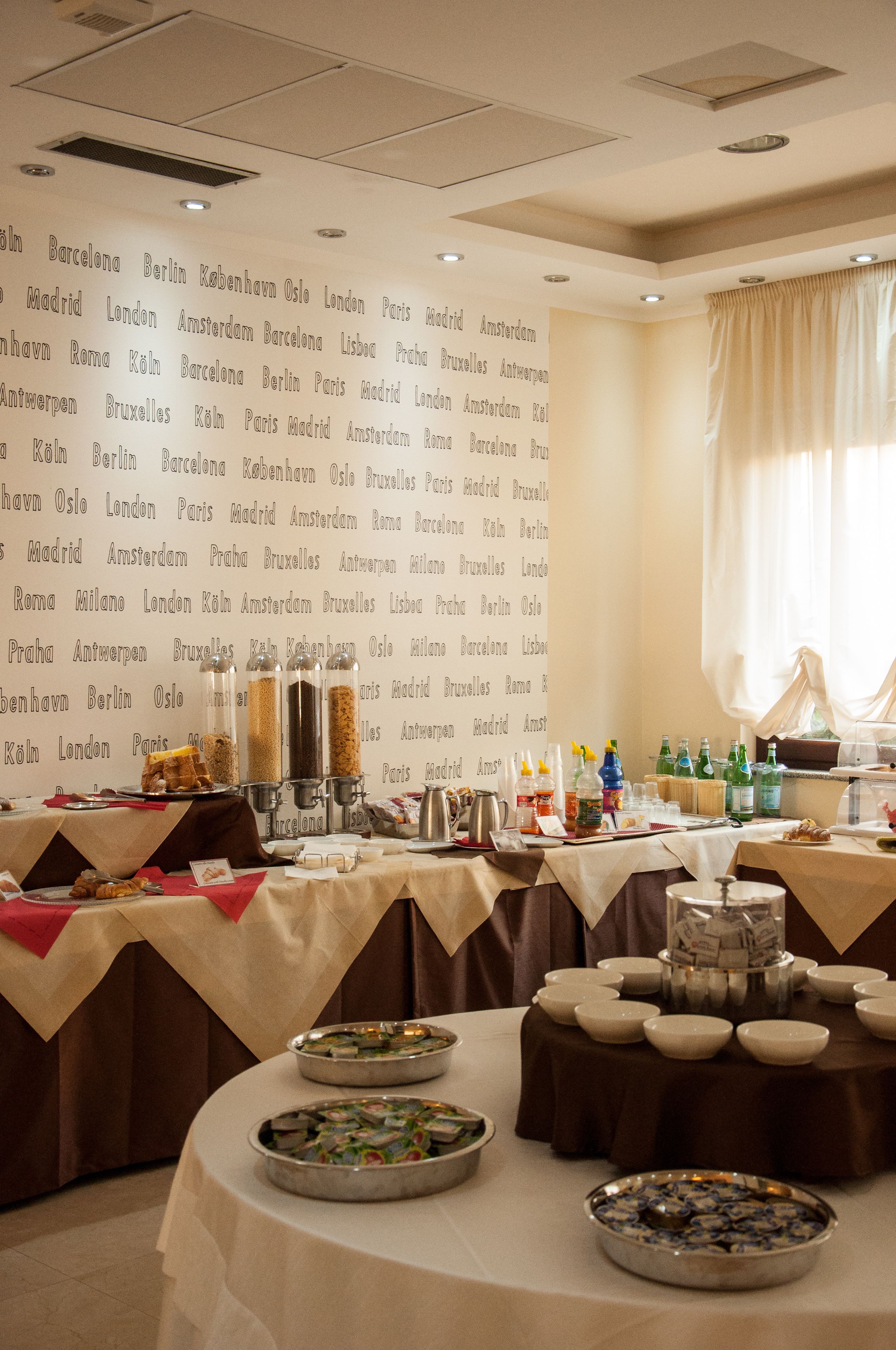 Sala de conferências com mesas preparadas para uma reunião, incluindo placas de identificação e diversos alimentos e bebidas.