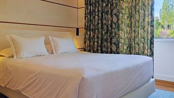 Uma cama bem arrumada com lençóis e almofadas brancas, um painel de cama com design geométrico e uma janela com cortinas florais.