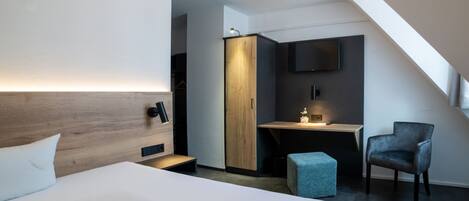 Quarto de hotel moderno com uma cama grande, uma escrivaninha, uma cadeira e uma TV fixada na parede.