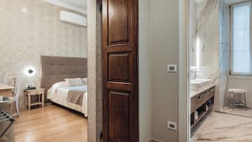 Um quarto com porta de madeira, uma cama com cabeceira, mesa de cabeceira e apoio para luminária.