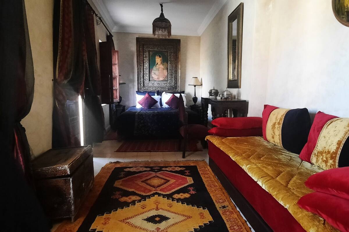Quarto com sofá, tapete estampado, baú de madeira e cama com almofadas.