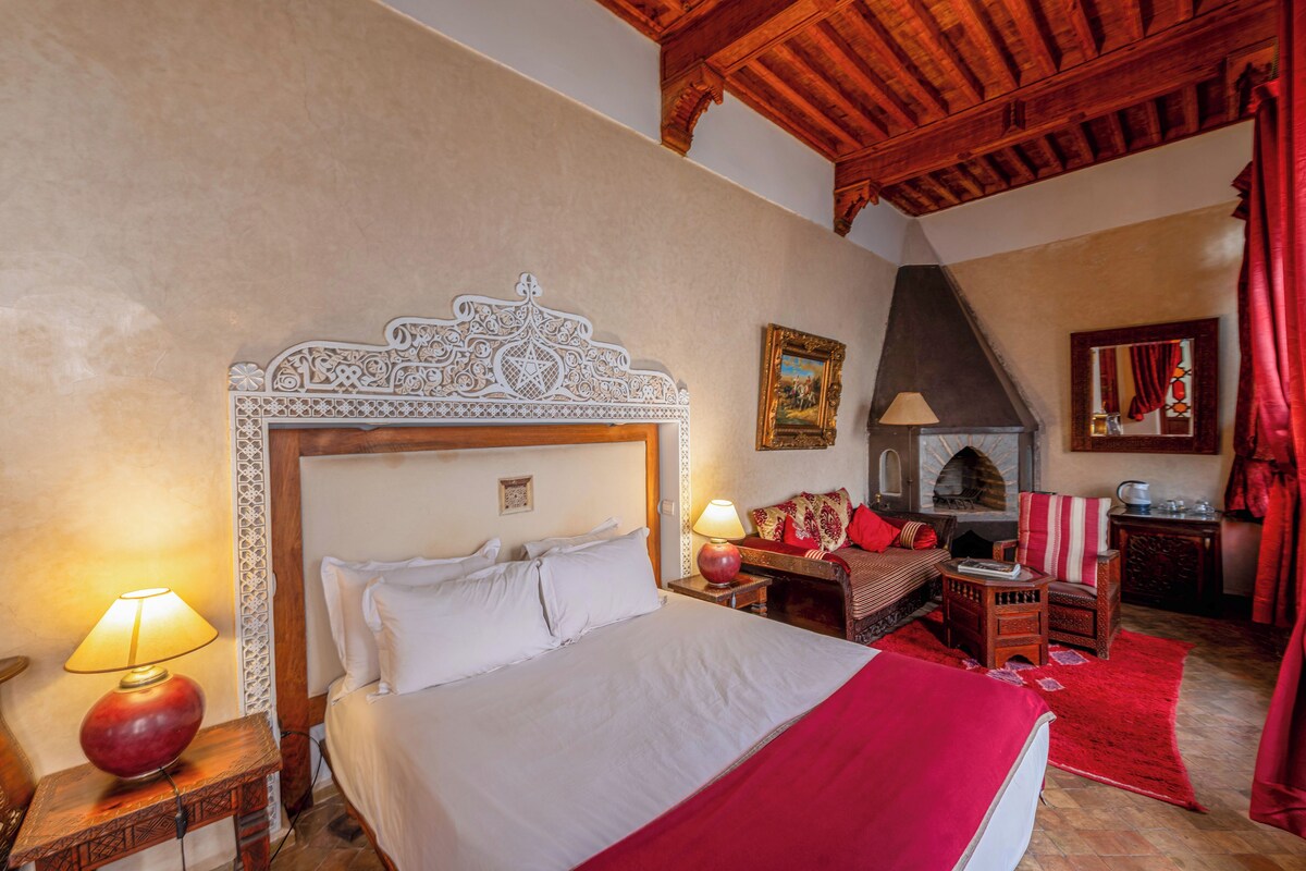 Quarto com cama grande, teto de madeira, lareira e cortina vermelha.