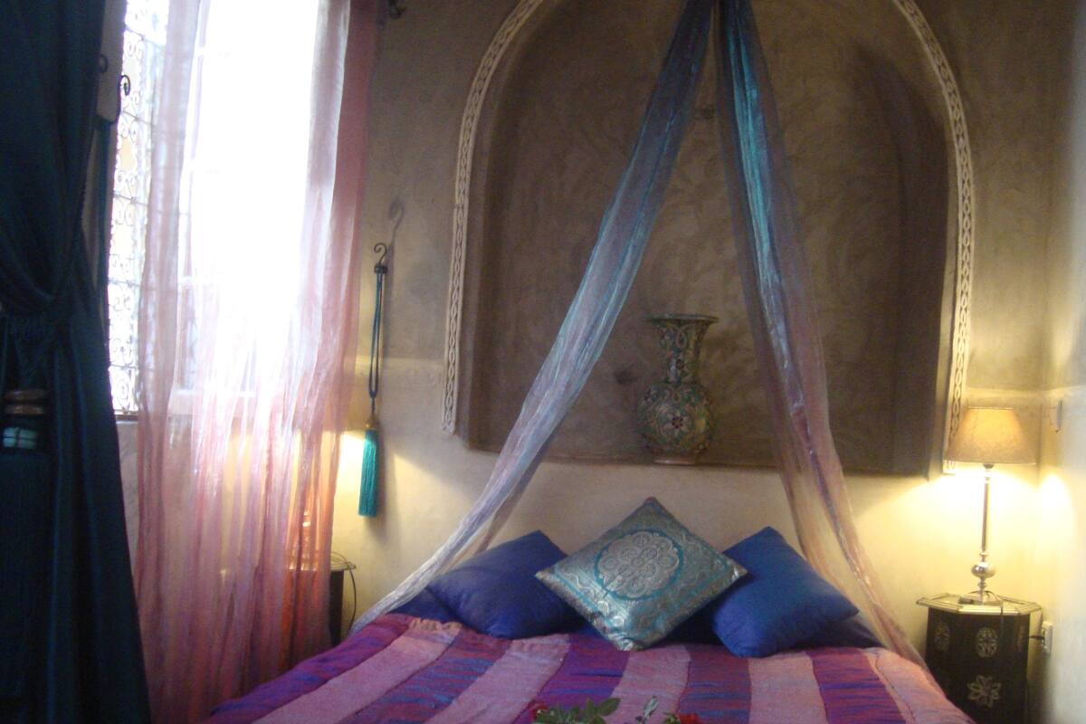 Quarto com cama, mesa de cabeceira, abajur e um objeto decorativo na parede.
