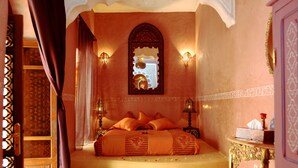 Quarto com cama, duas arandelas, espelho e uma mesinha com um vaso.