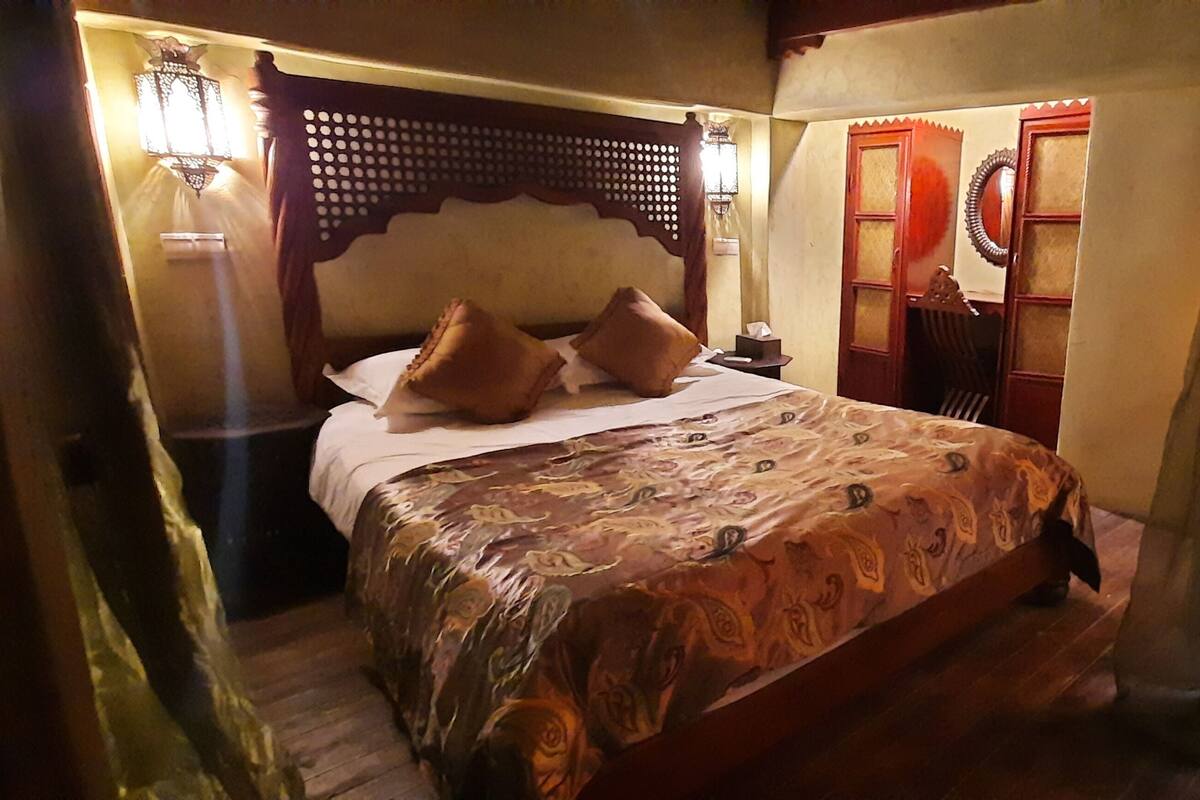 Quarto tradicional com cama, cabeceira de madeira e janela com cortinas.