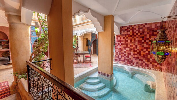 Uma área de piscina com chão ladrilhado, uma escadaria que leva a uma sala de jantar e um candeeiro decorativo.