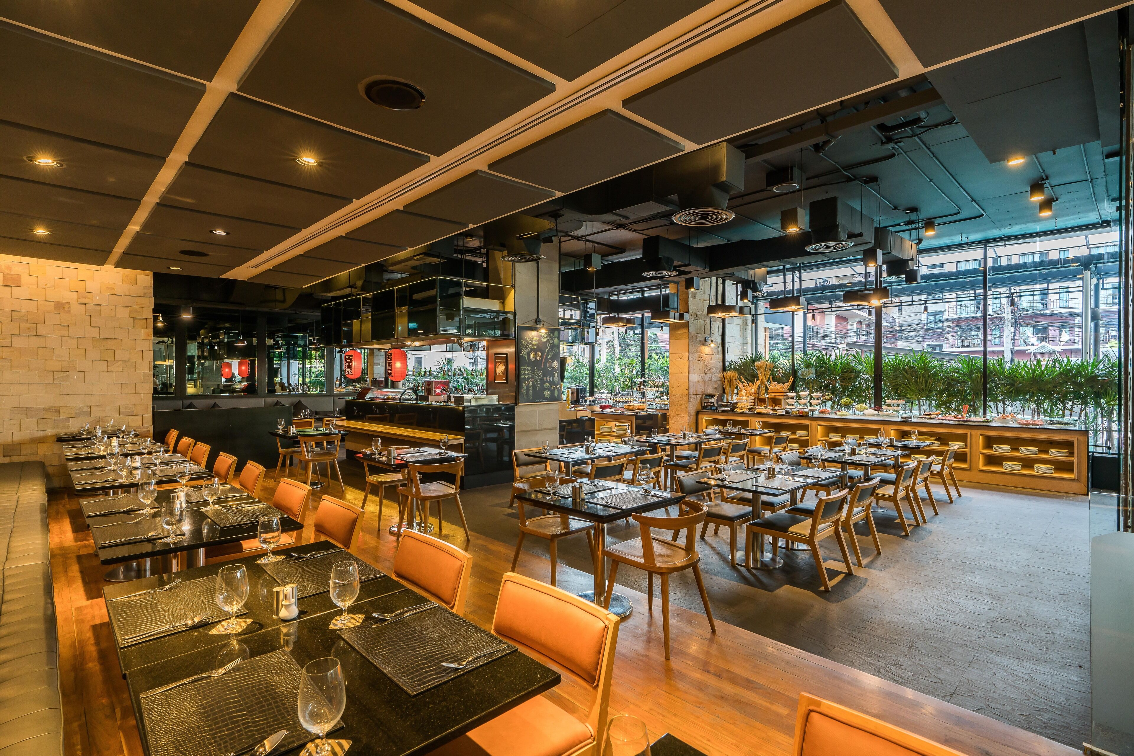Um restaurante moderno com mesas e cadeiras longas, um espaço de bar e grandes janelas com vista para o exterior.