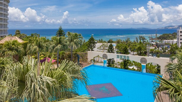 Um hotel com piscina, palmeiras e vista para o oceano.