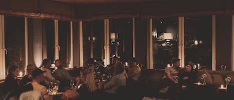 Um espaço com iluminação suave, grandes janelas, área de bar e disposição de assentos para hóspedes.