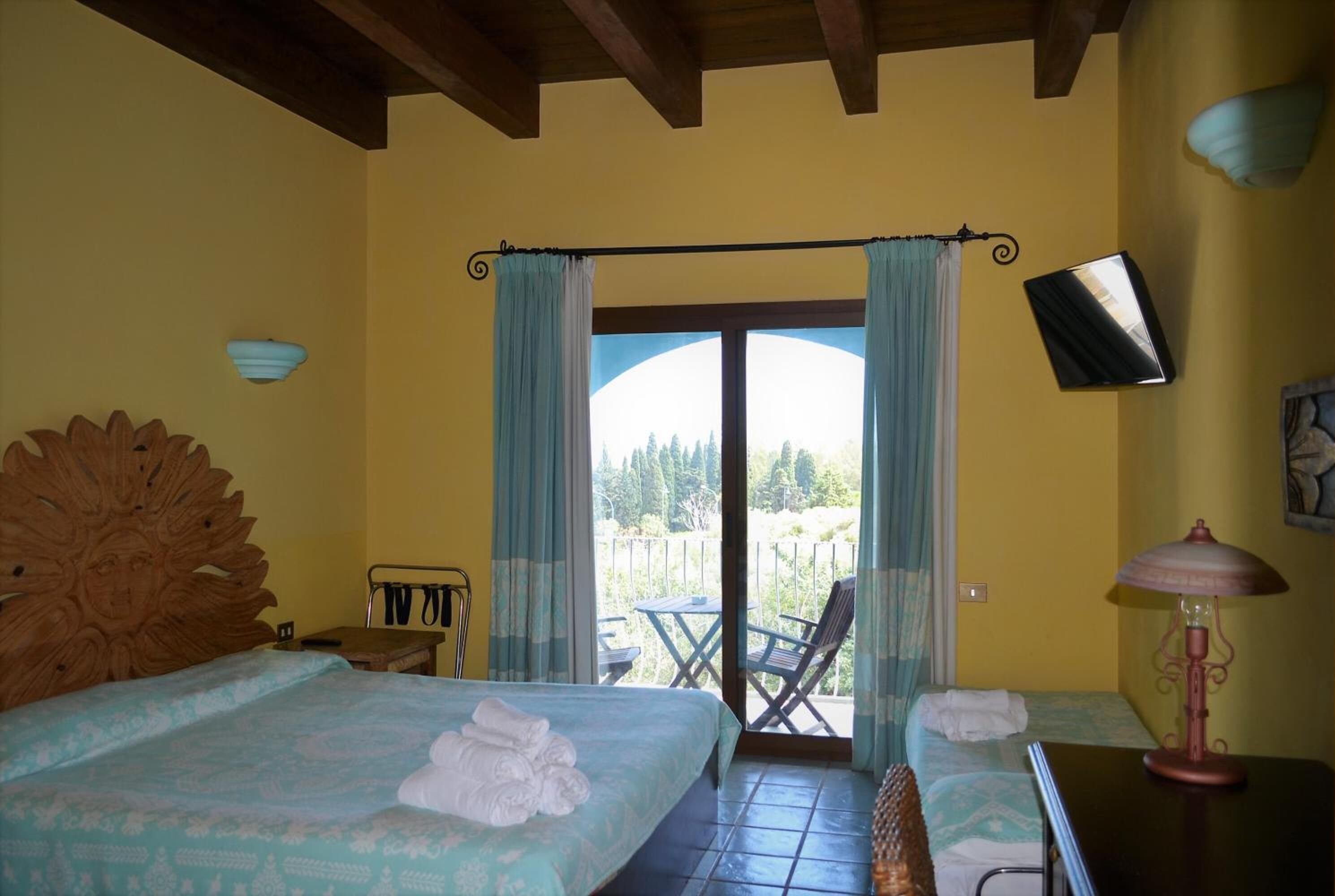 Quarto de hotel com cama, poltrona, mesa e varanda com vista para árvores.