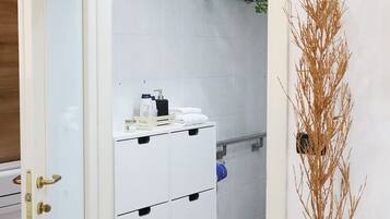 Casa de banho com lavatório branco, porta-toalhas e um vaso preto com plantas secas.