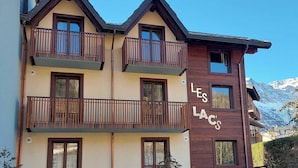 Um hotel com vários andares e varandas, vista para a montanha, e o nome 'LES LAC'S' na fachada.