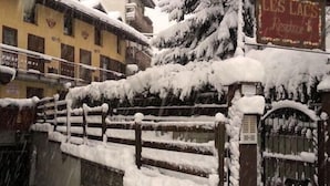 Rua coberta de neve com um portão de madeira e uma placa que diz 'LES LACS Resistance'.
