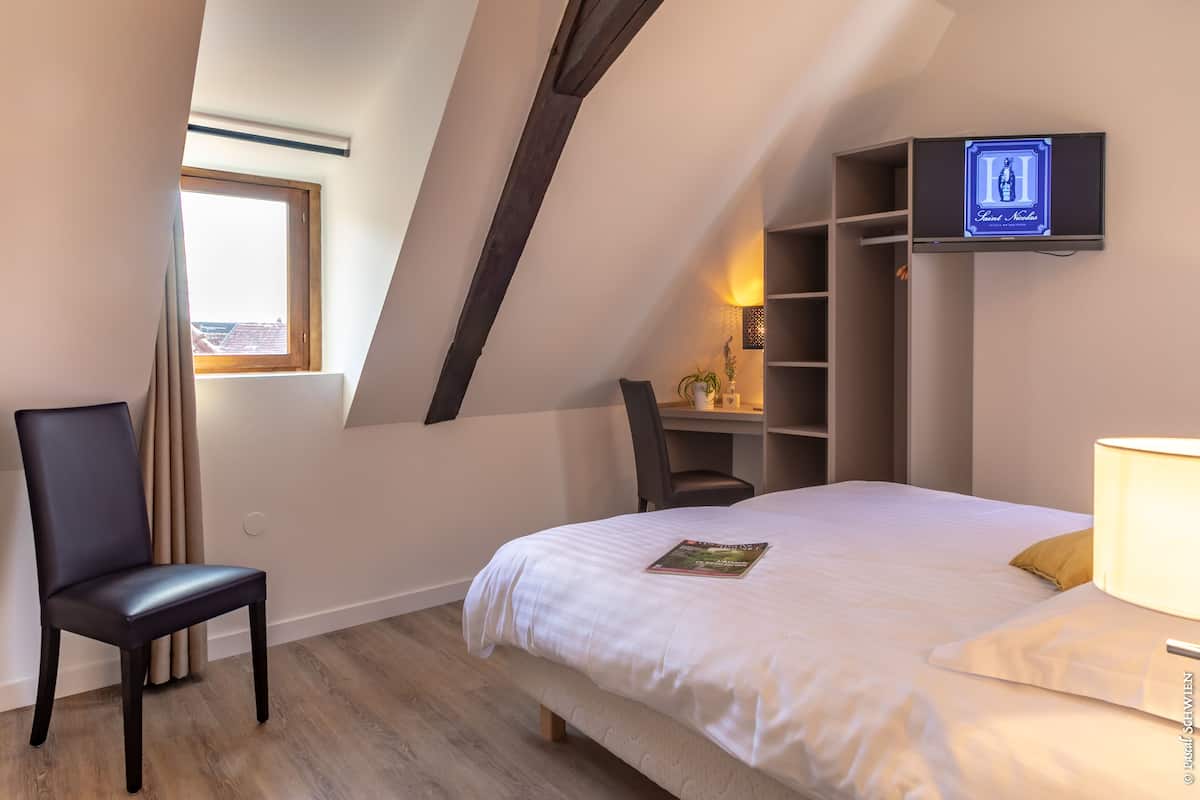 Quarto com uma cama, uma cadeira, uma escrivaninha, uma televisão e uma janela.