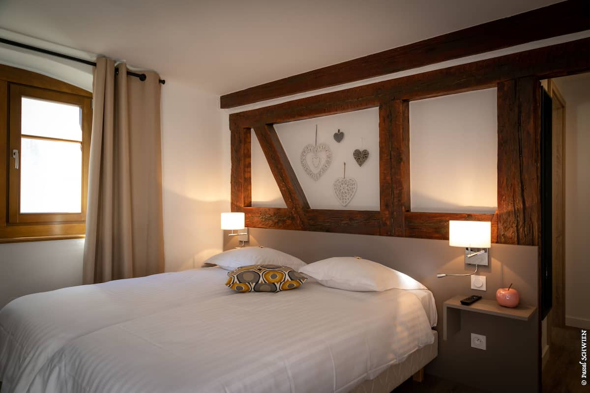 Cama bem arrumada com almofadas estampadas, abajur e arte decorativa de coração na parede.