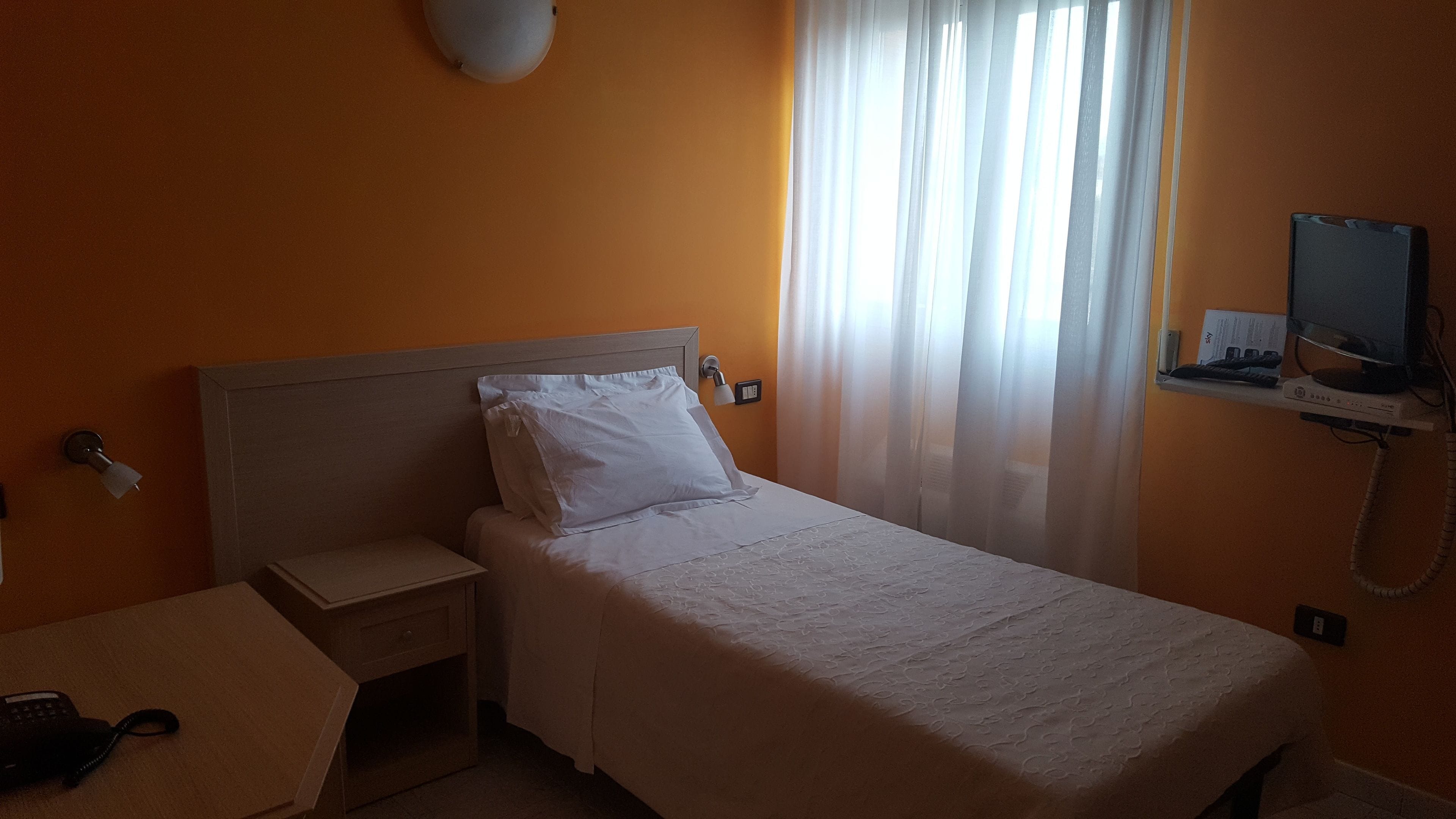 Quarto de hotel com uma cama, mesa de cabeceira, telefone e televisão.