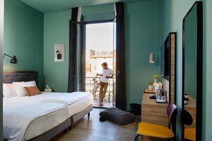 Quarto de hotel com cama, escrivaninha, cadeira, varanda e vista para edifícios.