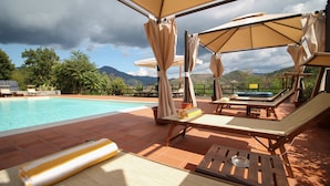 Uma área à beira da piscina com espreguiçadeiras, guarda-sóis e vista para as montanhas.