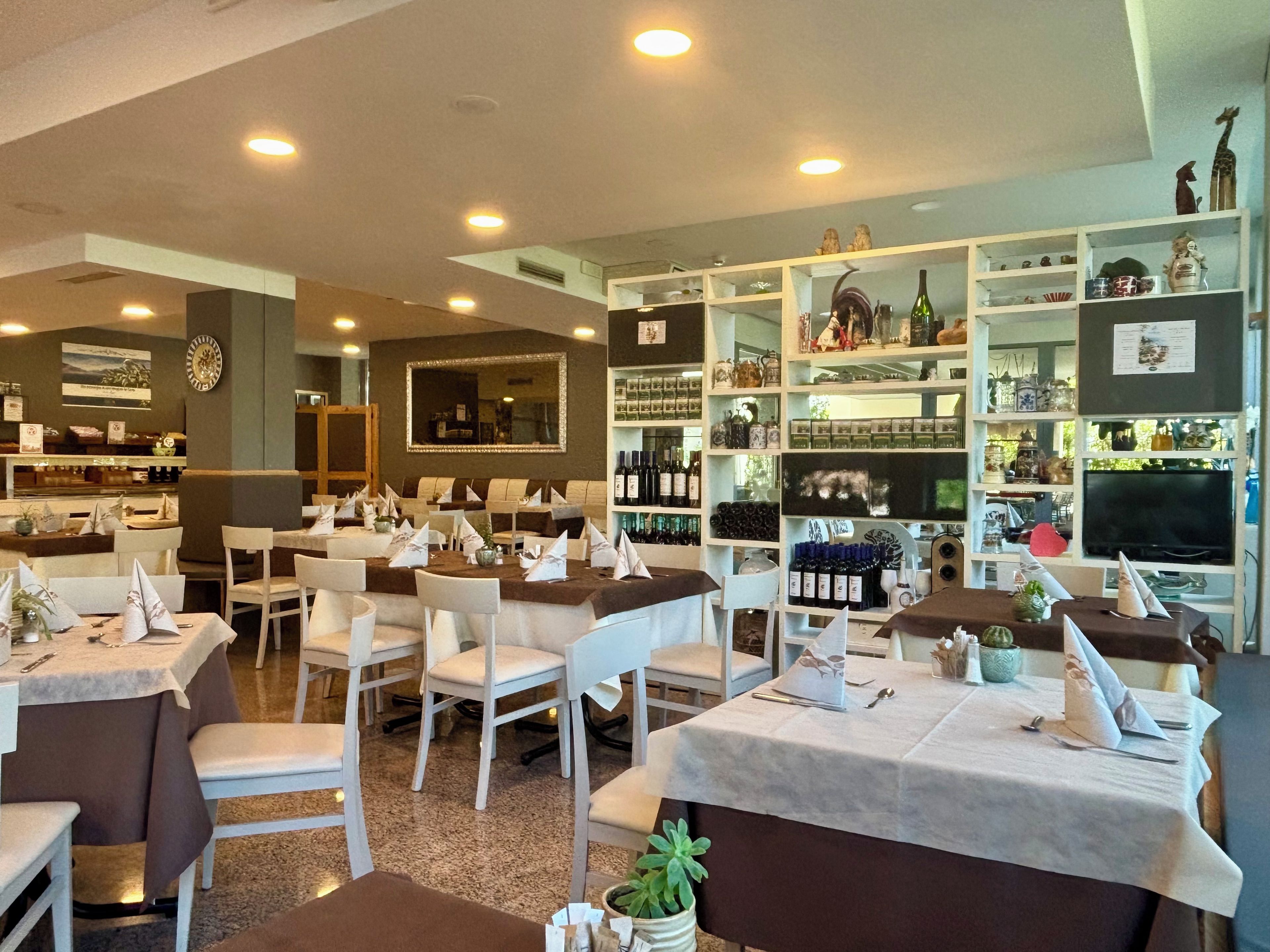 Interior de restaurante com várias mesas, cadeiras e prateleiras repletas de garrafas e objetos decorativos.