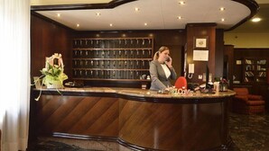 Uma receção com uma recepcionista atrás do balcão, uma estante grande e uma cadeira vermelha à direita.