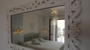Quarto com um espelho grande e trabalhado, cama com almofadas, mesa de cabeceira e luminárias fixadas na parede.