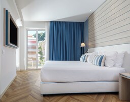 Quarto de hotel moderno com uma cama grande, uma TV fixada na parede e vista para a cidade pela janela.
