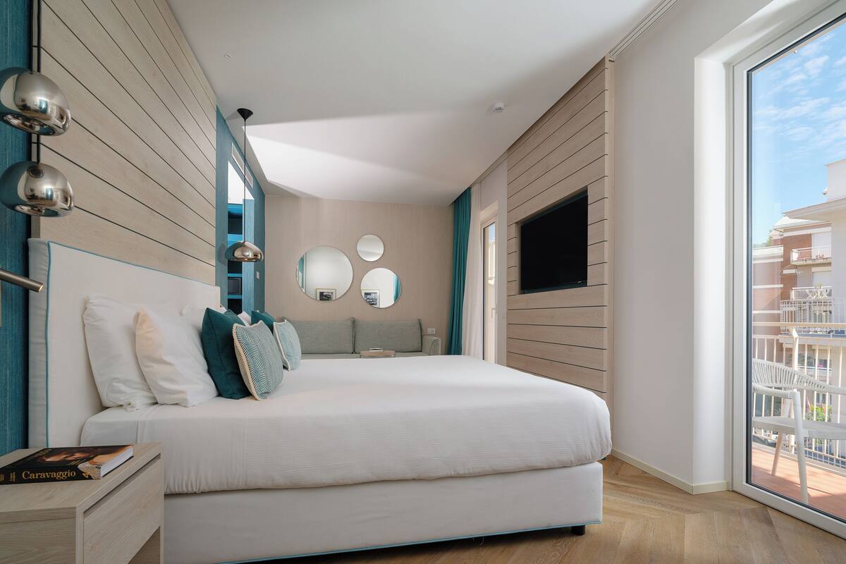 Quarto moderno com uma cama grande, mesas de cabeceira, uma televisão e vista para o exterior.