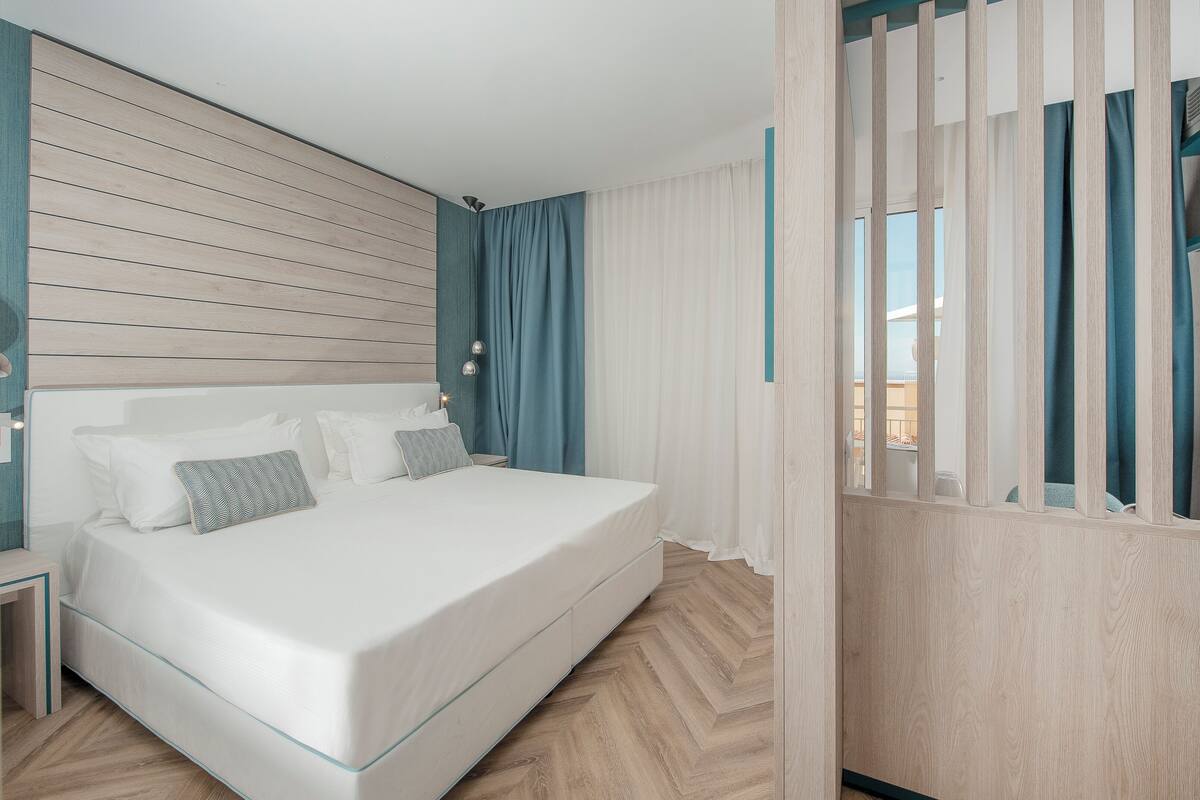 Quarto de hotel moderno com uma cama grande, painel de cabeceira em madeira e vista para o exterior.