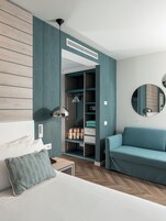 Quarto com cama, mesa de cabeceira, sofá azul, guarda-roupa e espelho.