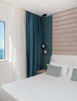 Quarto de hotel moderno com uma cama grande, mesa de cabeceira, abajur e vista para o oceano.