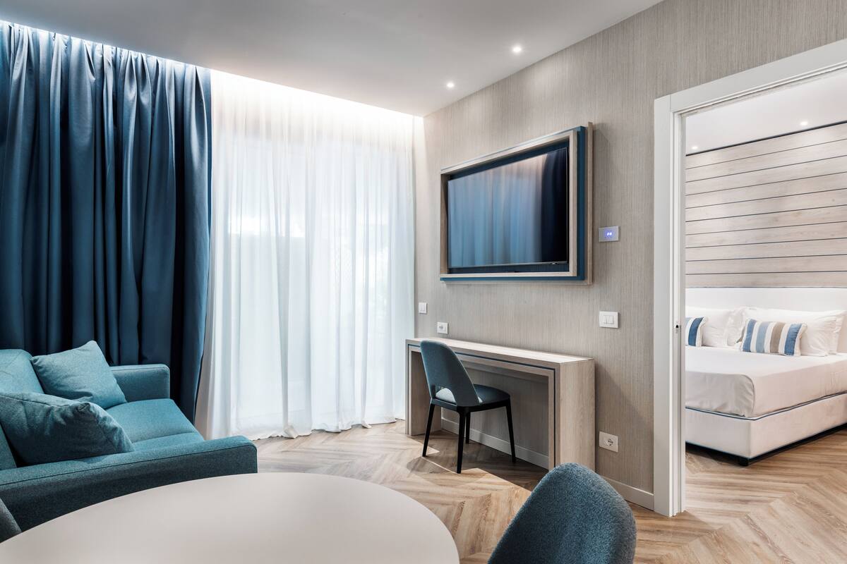 Quarto de hotel moderno com sofá, escrivaninha, televisão e cama.