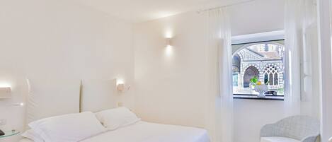 Quarto de hotel com cama, uma cadeira, janela com vista para um edifício e piso estampado.