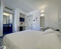 Quarto de hotel com uma cama, banheiro com pia, espelho e televisão na parede.