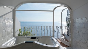 Casa de banho com uma banheira grande, vista para o mar e varanda com guarda-corpo.