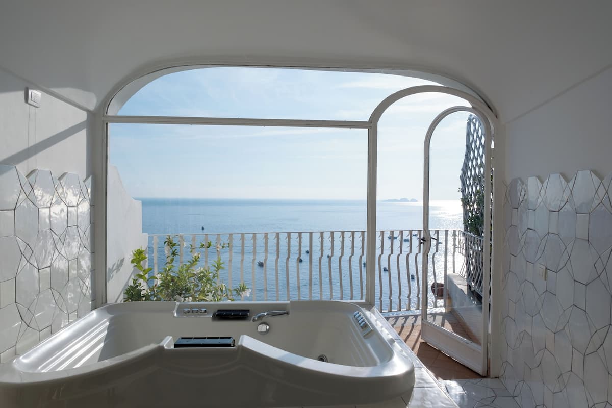Casa de banho com uma banheira grande, vista para o mar e varanda com guarda-corpo.
