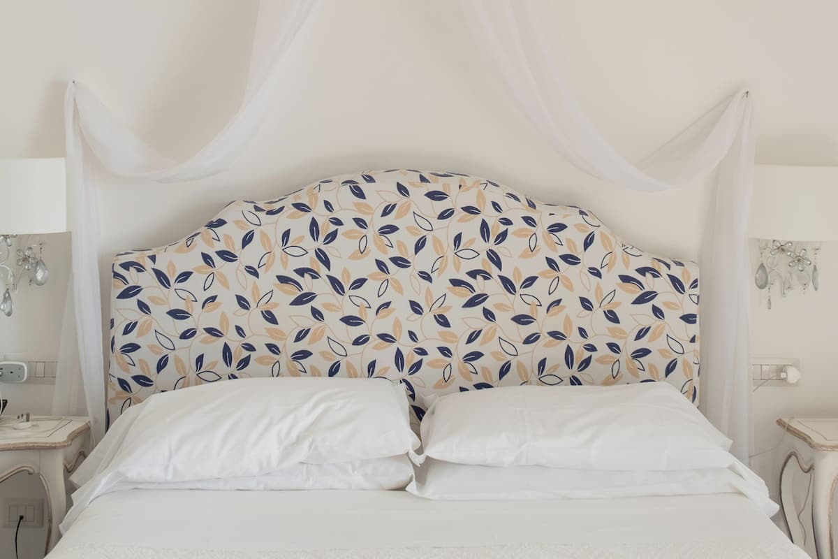 Uma cama com dossel e cabeceira estampada, duas mesas de cabeceira e luminárias fixadas na parede.