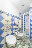 Um banheiro com piso azul e branco quadriculado, vaso sanitário branco, bidê e área de chuveiro.
