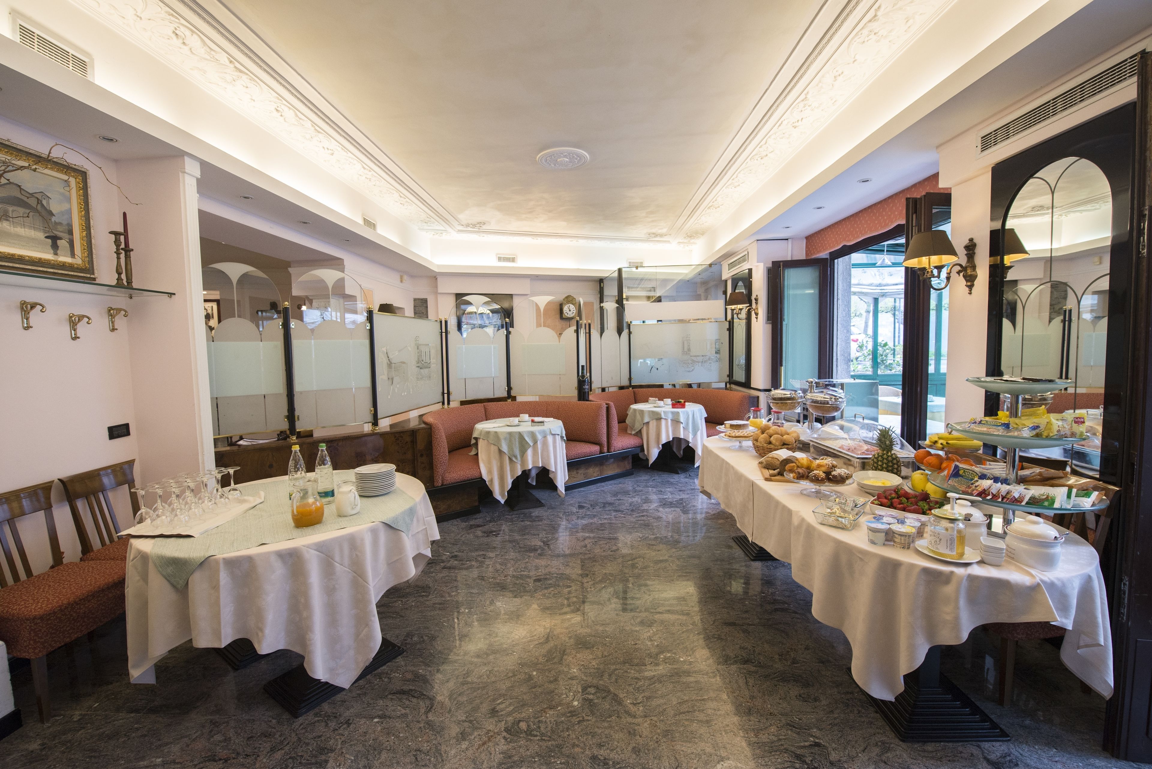 Uma área de refeições com várias mesas, assentos acolchoados e um buffet com diversos alimentos.