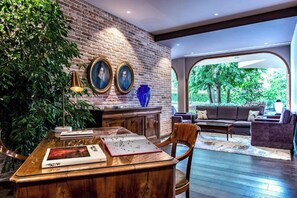 Uma sala de estar moderna com parede de tijolos, uma mesa de jantar com livros e uma grande janela com vista para vegetação.