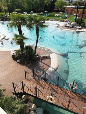 Área de piscina com espreguiçadeiras, palmeiras e deck de madeira.