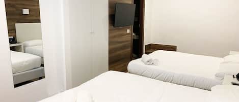 Quarto de hotel com duas camas, um guarda-roupa, uma TV presa na parede e uma TV de tela plana no aparador.