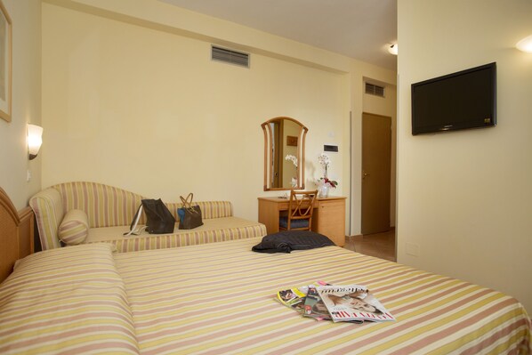 Quarto de hotel com duas camas, uma escrivaninha, uma cadeira, uma televisão e um espelho.