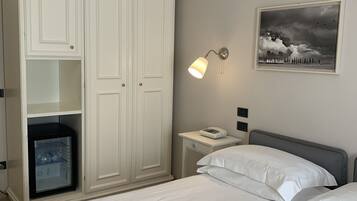 Quarto com cama, guarda-roupa, mesa de cabeceira com abajur e um quadro na parede.