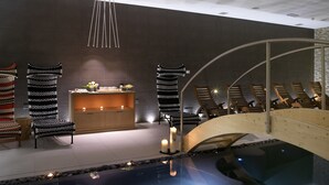 Uma área de piscina interior moderna com espreguiçadeiras, um balcão de recepção e velas.