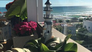 Uma varanda com vista para o oceano, uma réplica de farol e plantas em vasos.