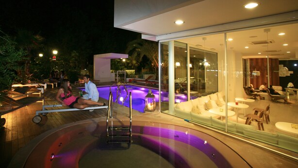 Uma área de piscina moderna ao ar livre, com uma estrutura de vidro, espreguiçadeiras e uma cascata.