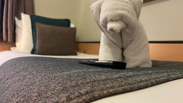 Quarto de hotel com uma cama, um controle remoto e um brinquedo macio sobre a cama.