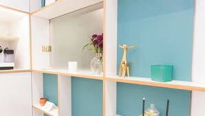 Um interior moderno com prateleiras brancas e azul-esverdeadas, um vaso com flores roxas e um objeto decorativo dourado.